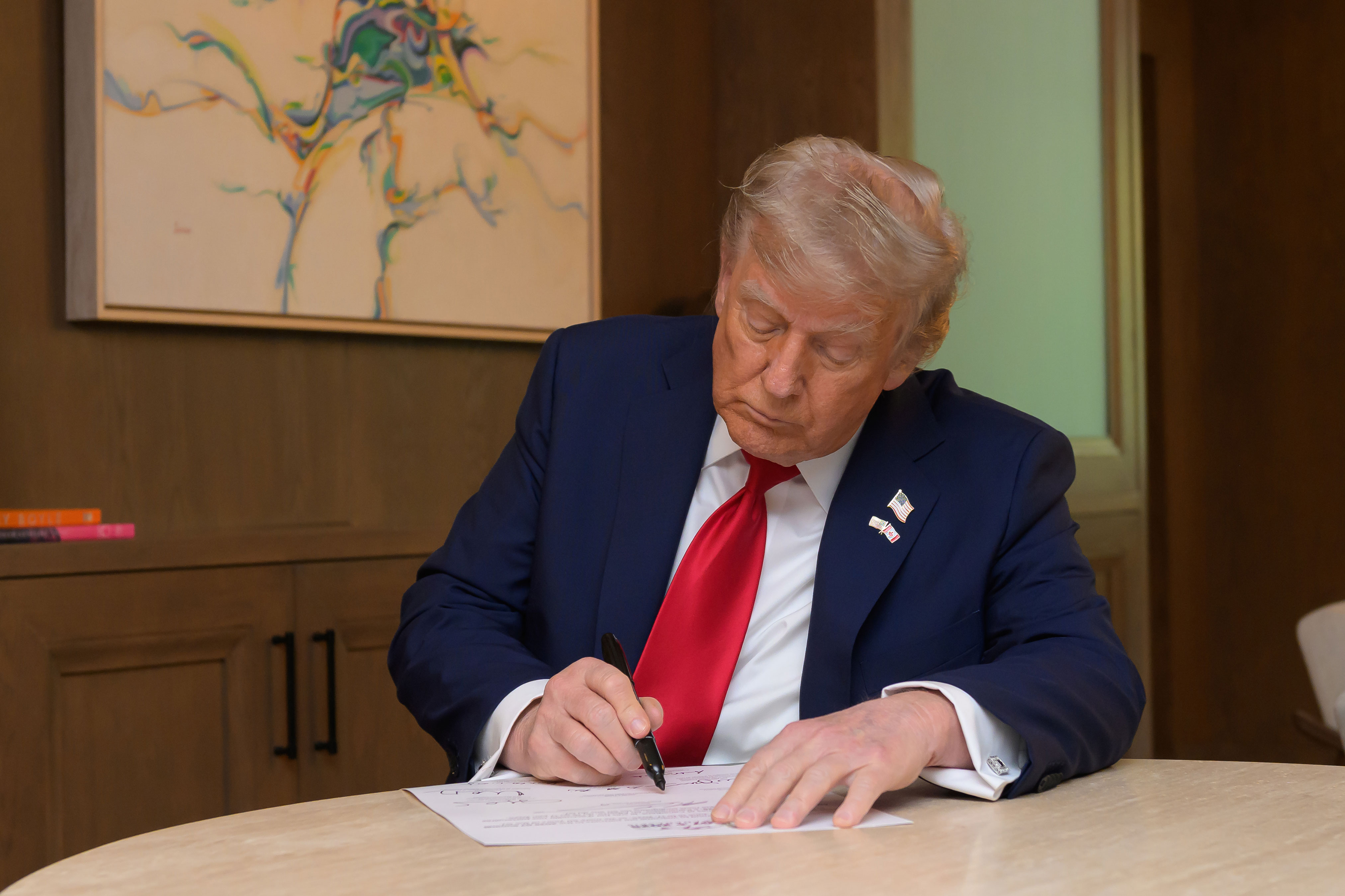 A man in a suit holding a pen and signing a piece of paper that is on a ...